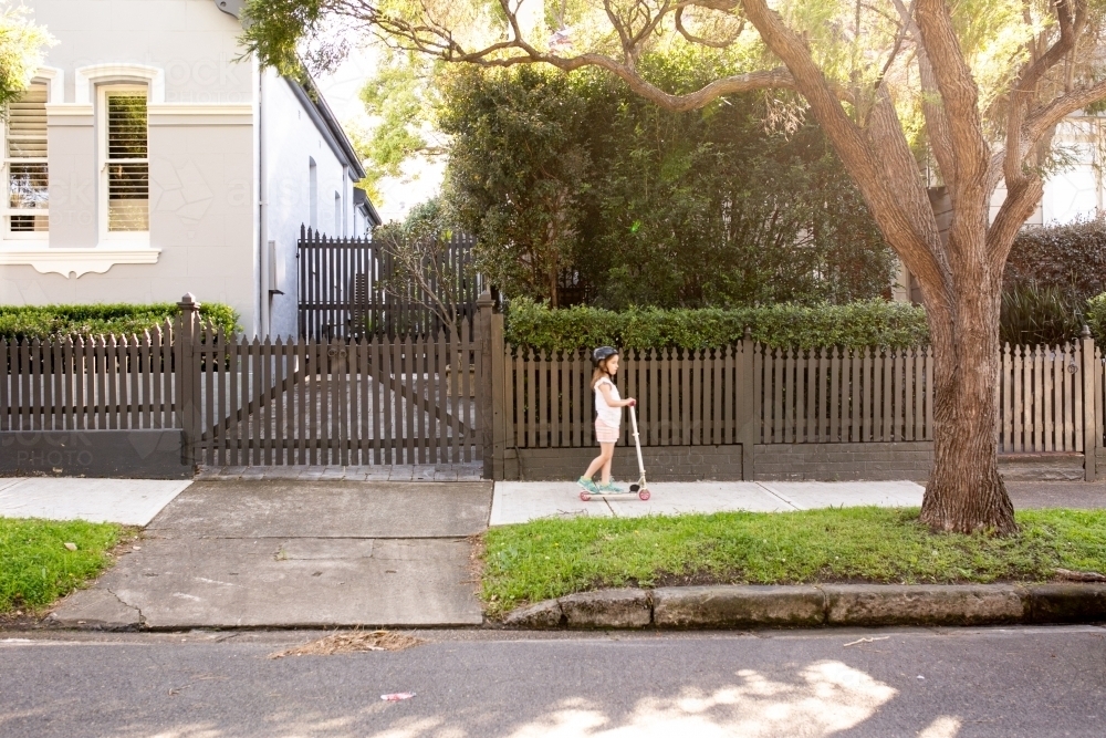 Image of girl riding on a scooter with helmet on the sidewalk with a ...