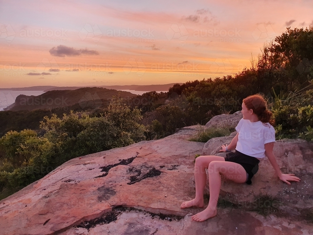 Image of Girl sitting on a rock looking at the sunset - Austockphoto