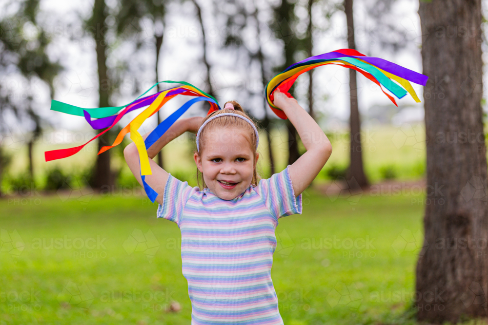 Image of Girl with rainbow streamers running around outside in country ...