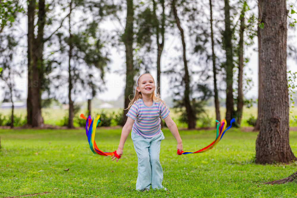 Image of Girl with rainbow streamers running around outside in country ...