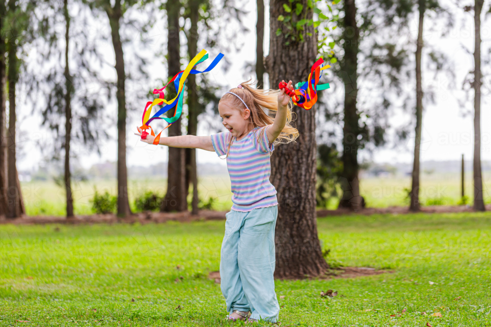 Image of Girl with rainbow streamers running around outside in country ...