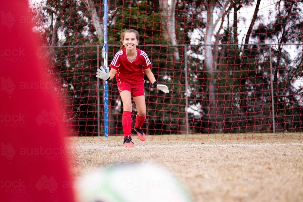 Image of Goal keeper wearing a red football team uniform defending the ...