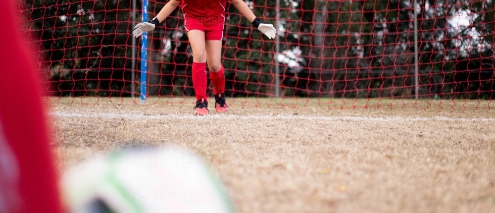 Image of Goal keeper wearing a red football team uniform defending the ...