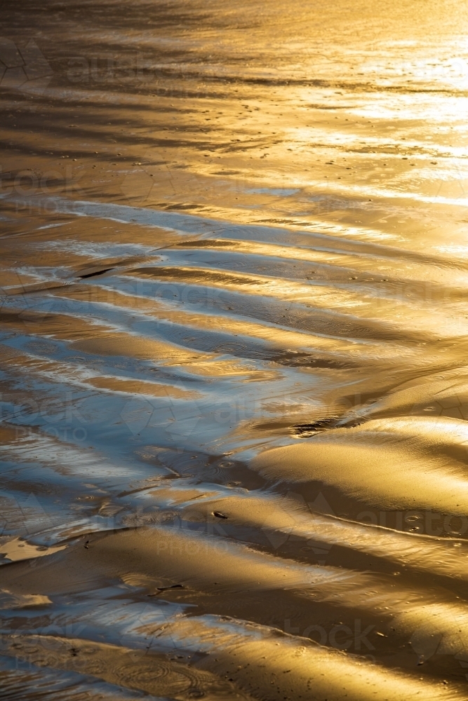 Image of Golden light reflecting off a rippled wet beach - Austockphoto