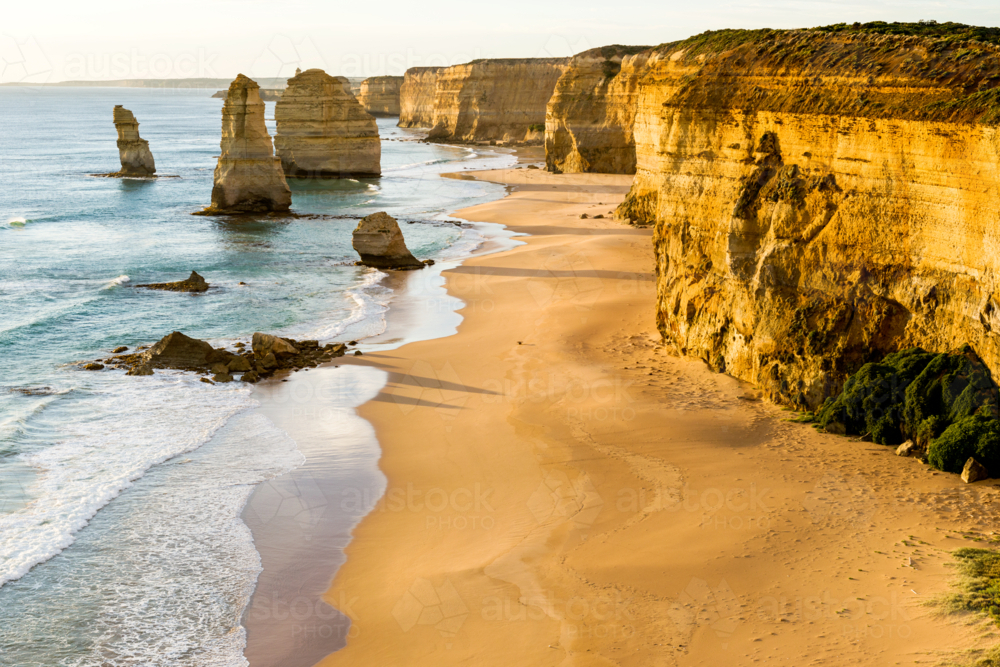 Image of Golden sandstone cliffs and sea stacks rise above a quiet ...