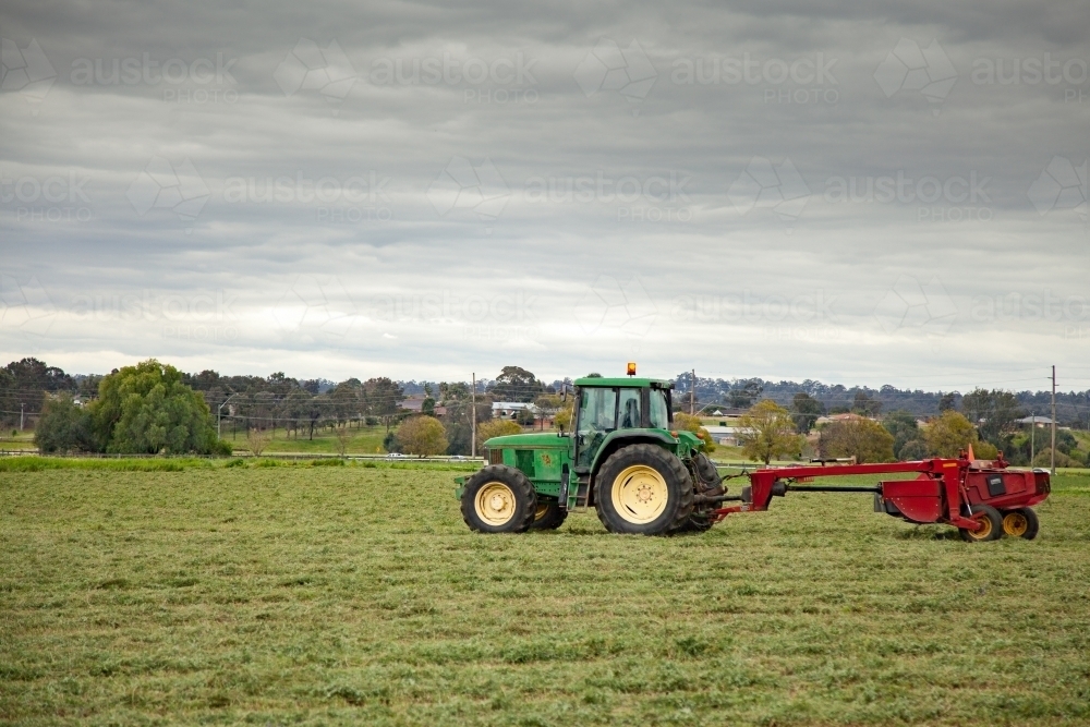 Image of Green tractor pulling red slasher in lucerne paddock ...