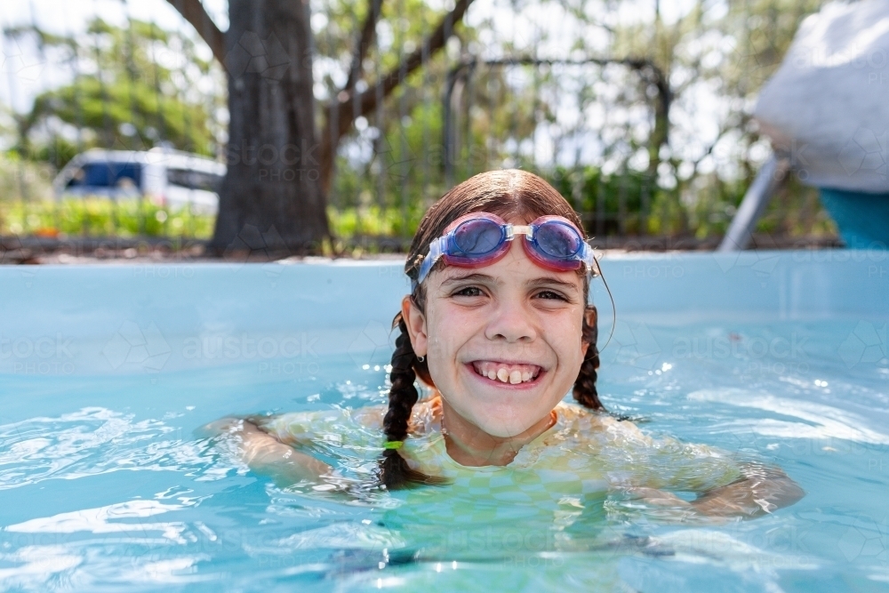Image of Grinning ten year old girl in backyard pool with goggles ...