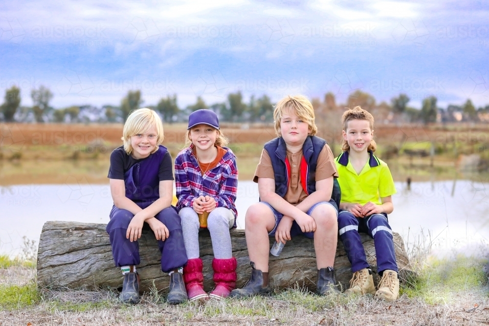 Image of Group of happy country kids sitting on log on farm with dam in ...