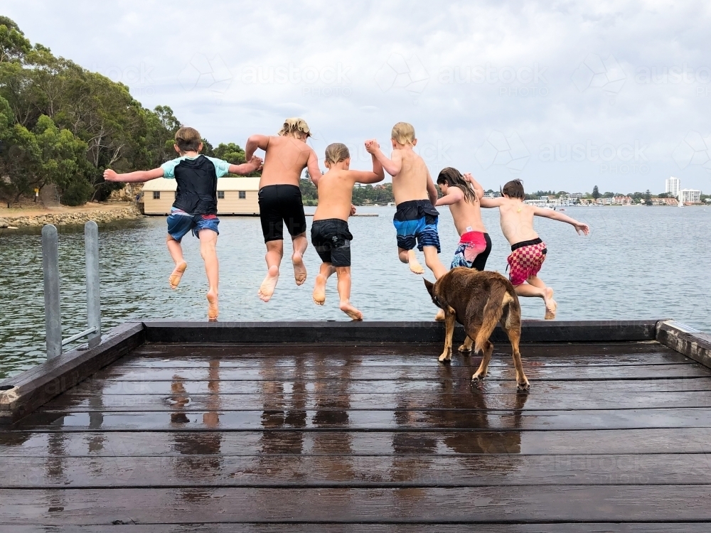 Image of Group of kids jumping off a wharf into the water - Austockphoto