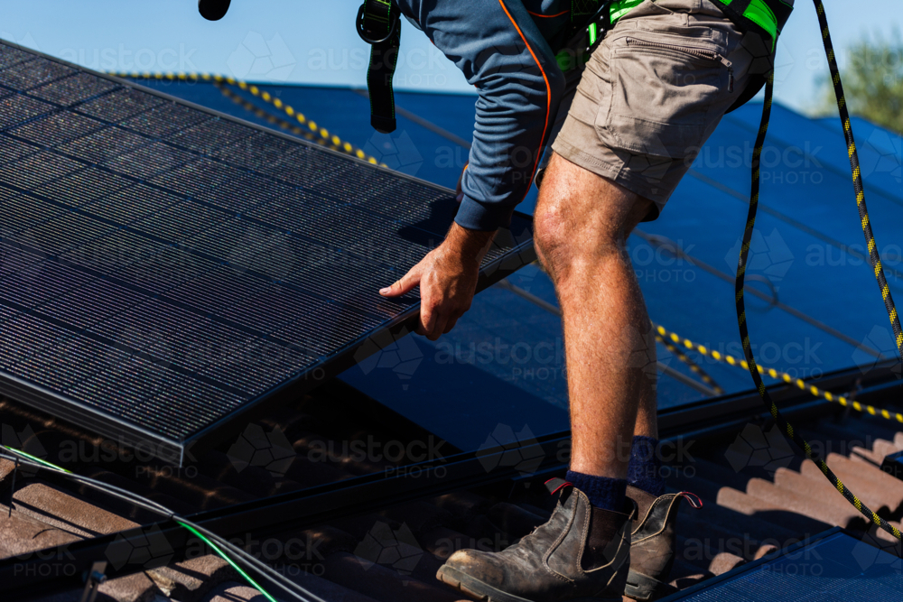 Image of Guy in shorts installing solar panels on hot sunlit roof ...