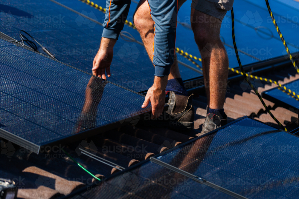 Image of Guy in shorts installing solar panels on hot sunlit roof ...