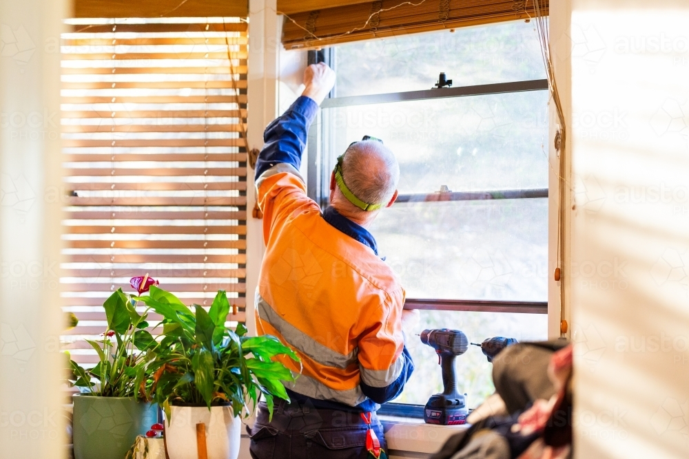 Image of Handyman tradie repairing window in home - Austockphoto