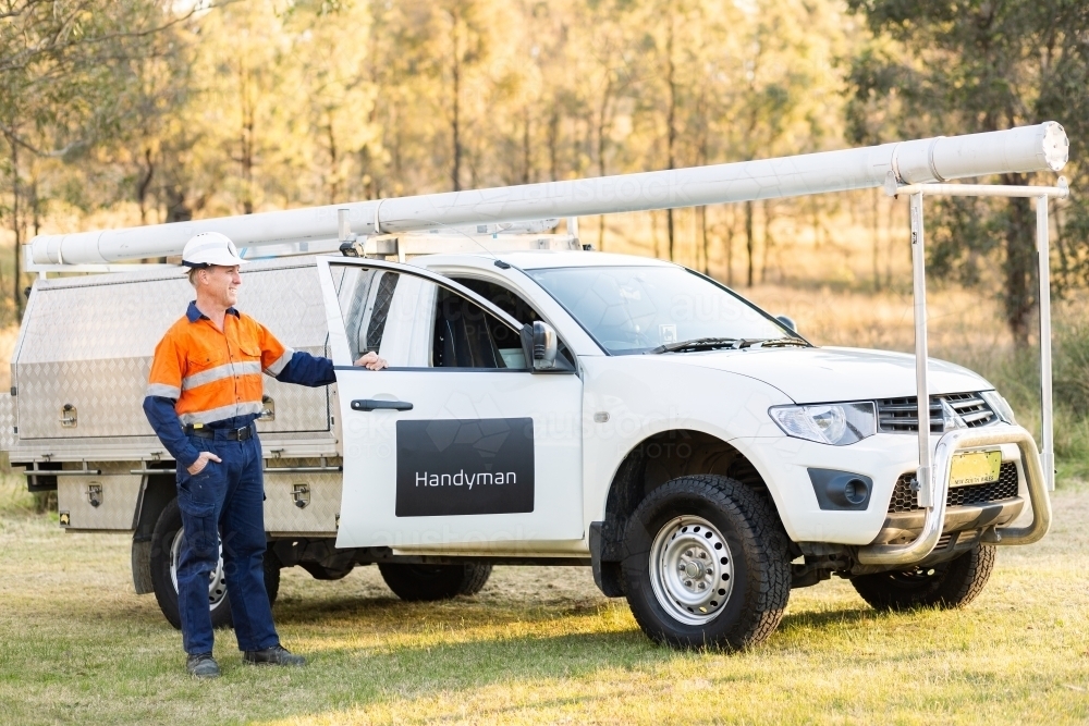Image of handyman with hard hat and high-vis workwear beside work ute ...