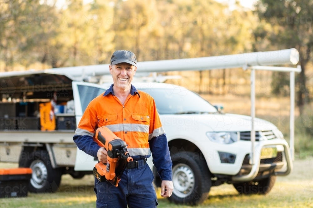 Image of Handyman with nail gun power tool beside tradie ute - Austockphoto