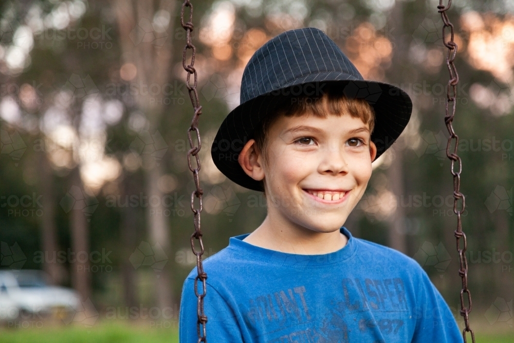 Image of Happy 9yo kid in a hat playing on swing outside - Austockphoto
