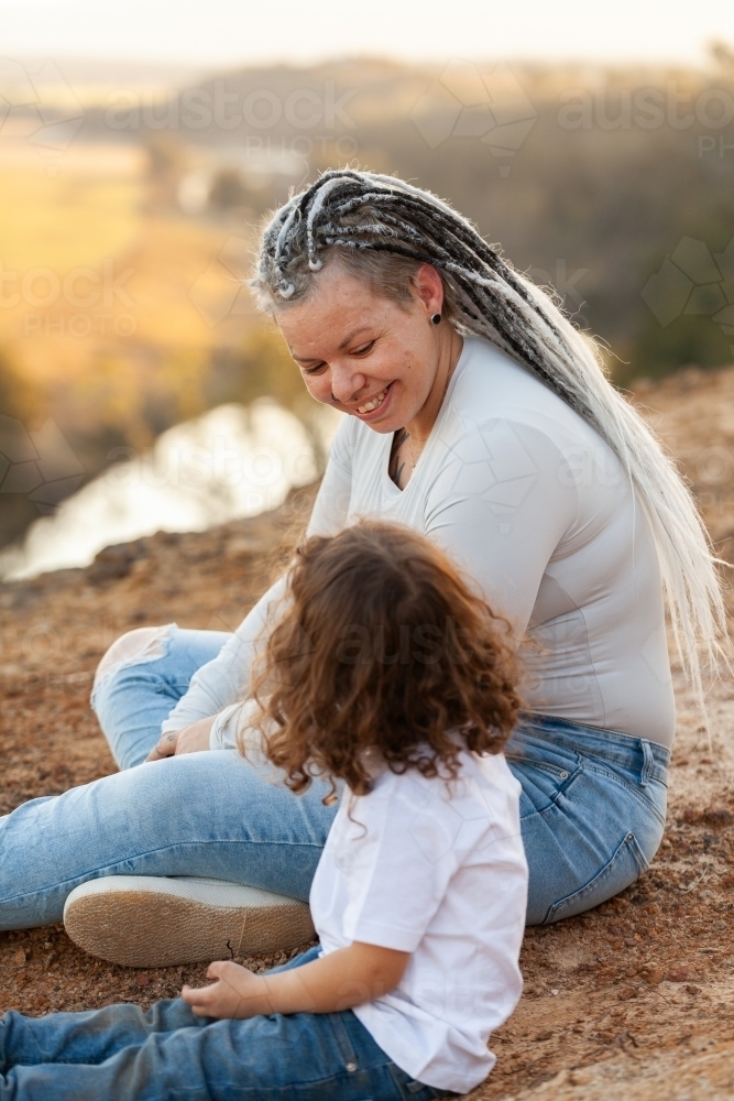 Image of Happy aboriginal mum with daughter sitting on cliff edge in ...