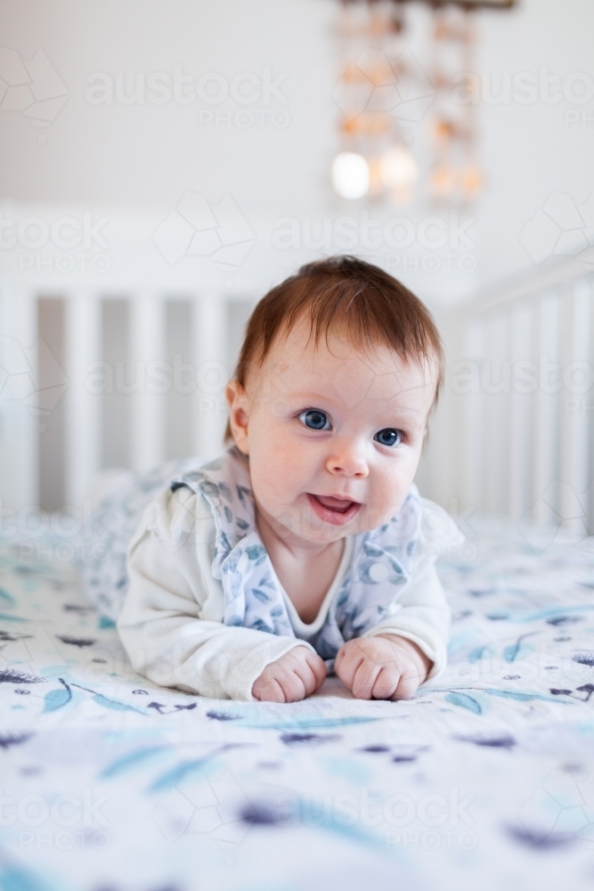 Image of Happy Aussie baby smiling at tummy time in cot in bedroom ...