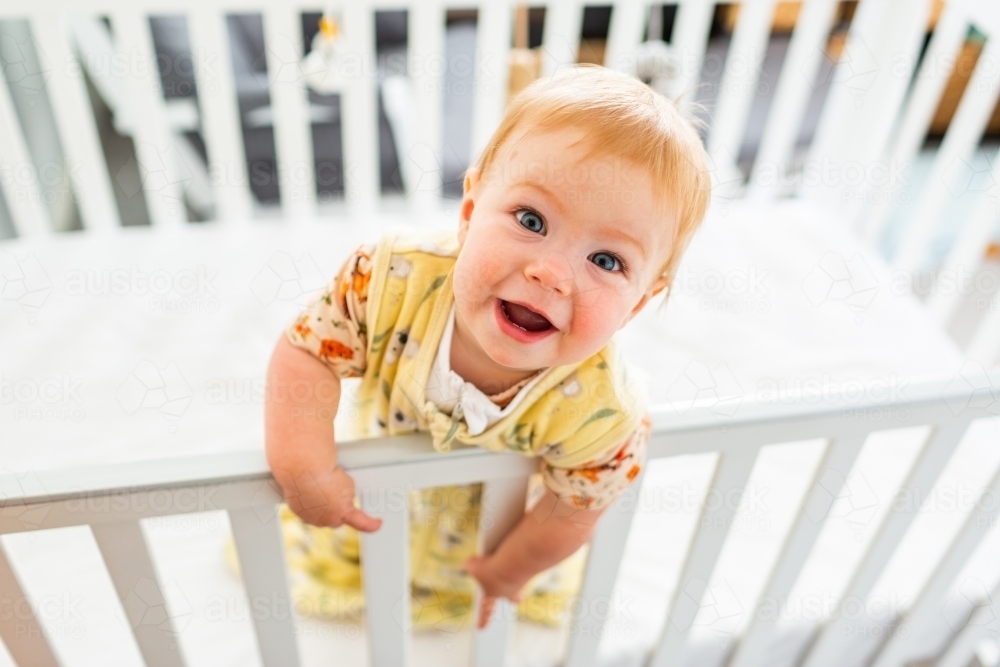 Image of Happy aussie baby smiling up at camera from cot in bedroom ...