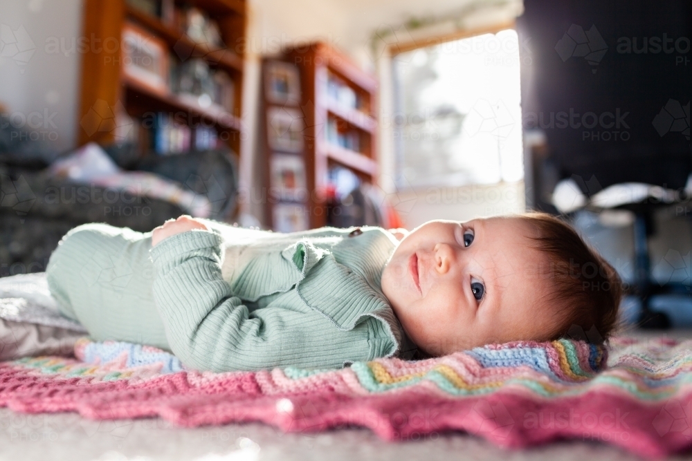 Image of happy baby girl lying on blanket on loungeroom floor in winter ...