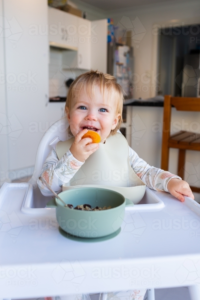 Image of Happy baby in high chair eating breakfast with peach half ...