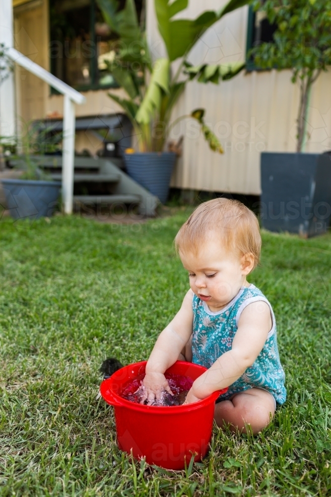 Image of Happy baby sitting splashing in red container of water and ...