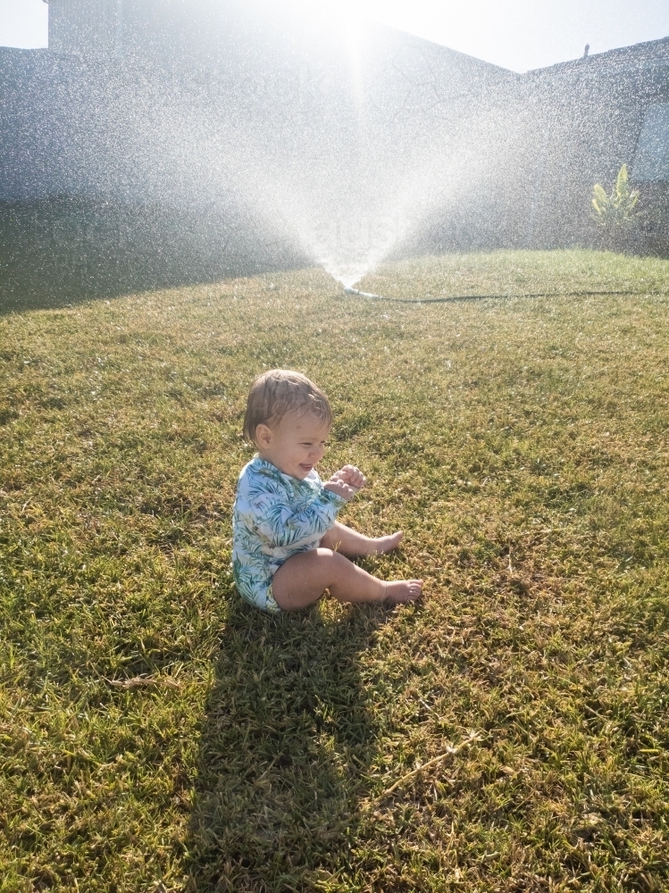 Image of Happy baby under spray of sprinkler in backyard as lawn is ...