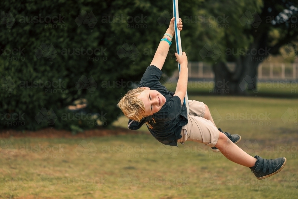 Image of Happy boy playing on swing at park - Austockphoto