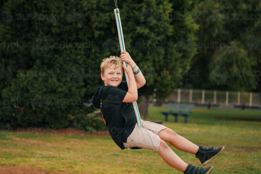 Image of Happy boy playing on swing at the playground - Austockphoto
