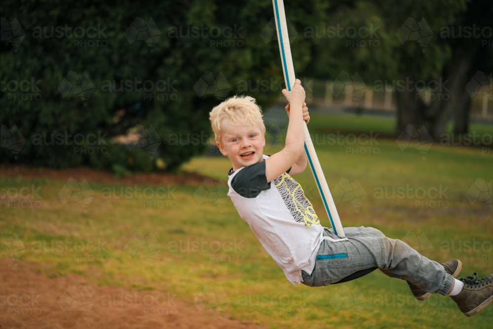 Image of Happy boy playing on swing at the playground - Austockphoto