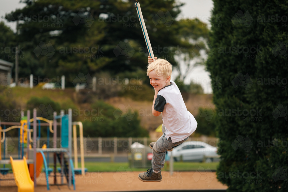 Image of Happy boy playing on swing at the playground - Austockphoto