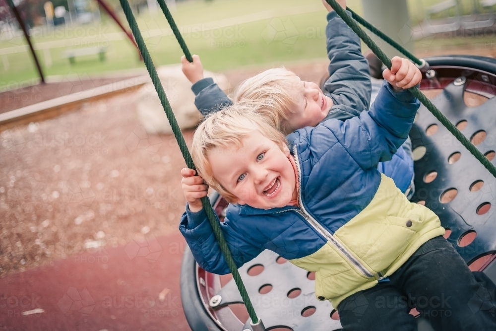 Image of Happy brothers playing on swing together at playground ...