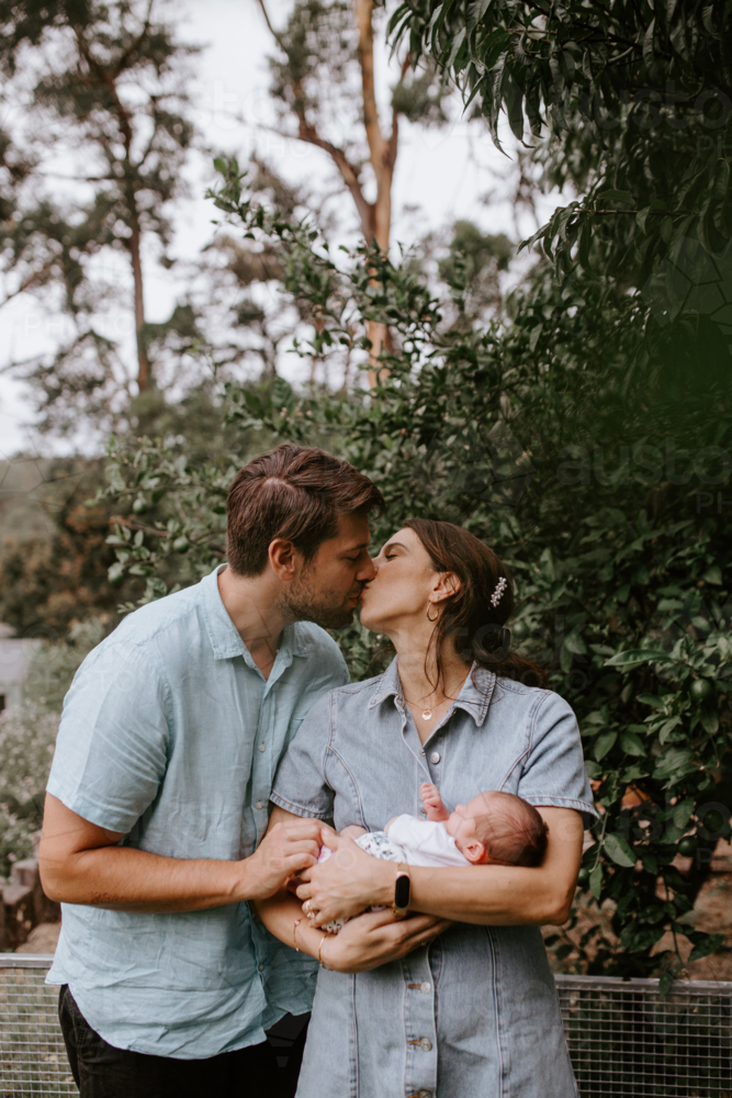 Image of Happy Caucasian couple kissing while holding their newborn ...