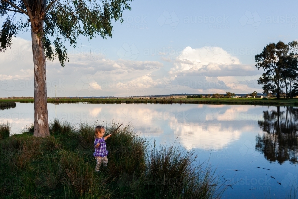 Image of Happy country child playing by dam on farm with stick at the ...