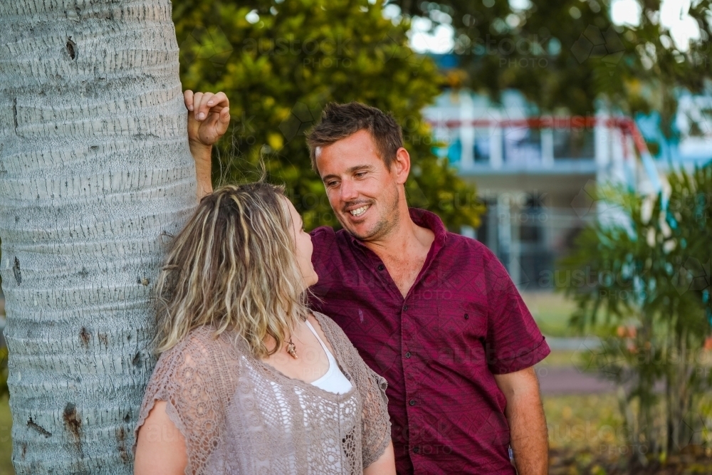 Image of Happy couple leaning against palm tree at the park - Austockphoto