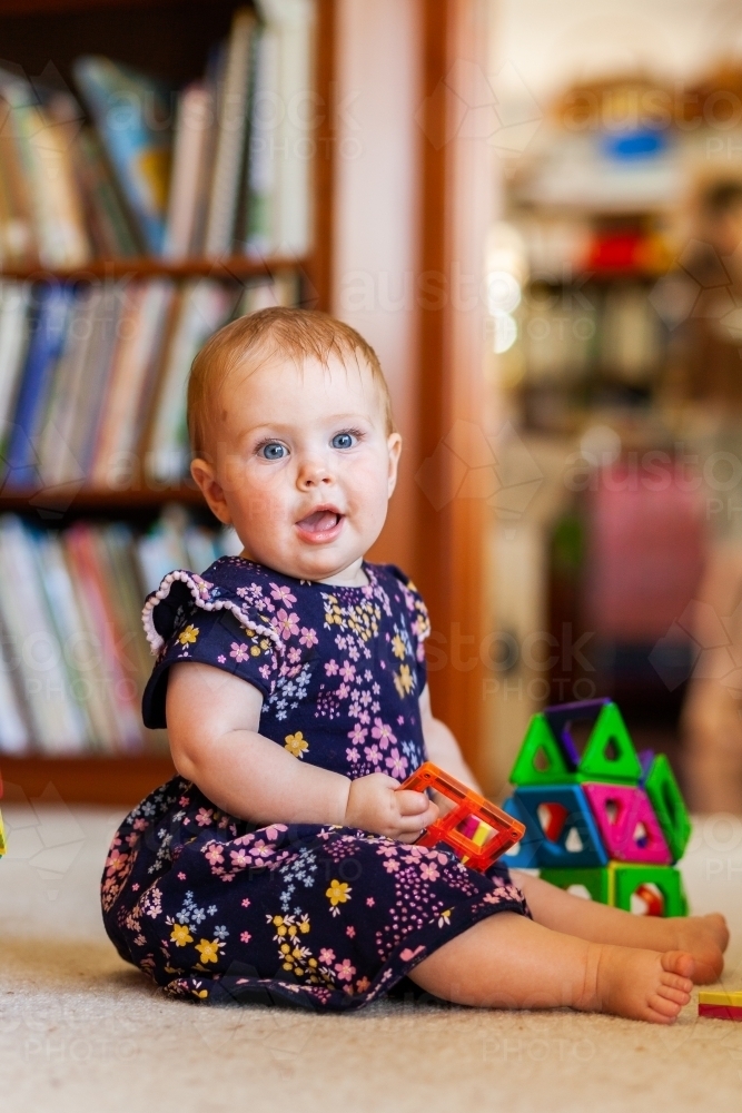 Image of Happy eight month old baby sitting on floor playing with ...