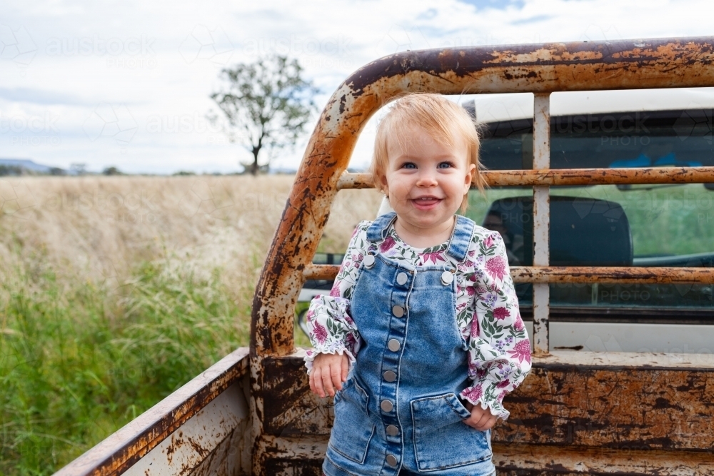 Image of Happy farm kid standing on back of ute in paddock on ...