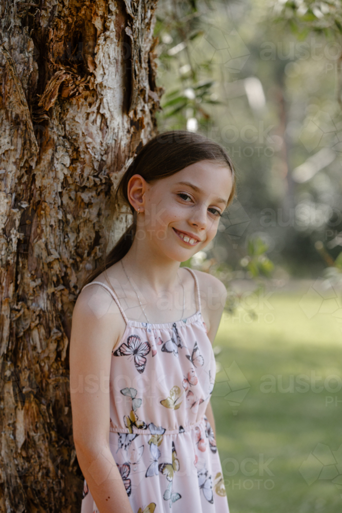 Image of Happy girl standing beside the tree trunk outdoors - Austockphoto
