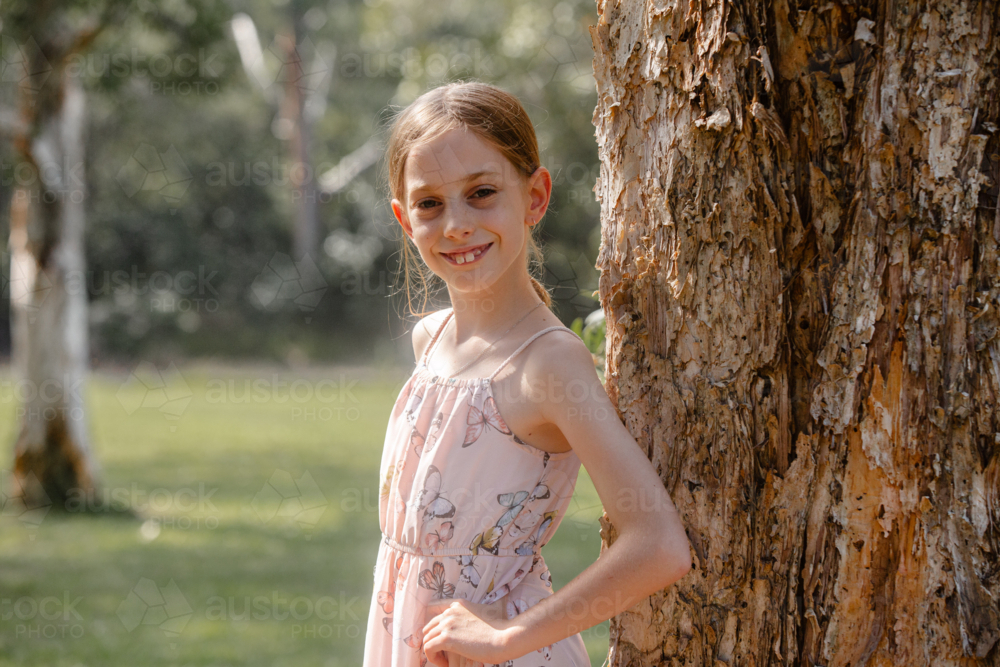 Image of Happy girl standing beside the tree trunk outdoors - Austockphoto