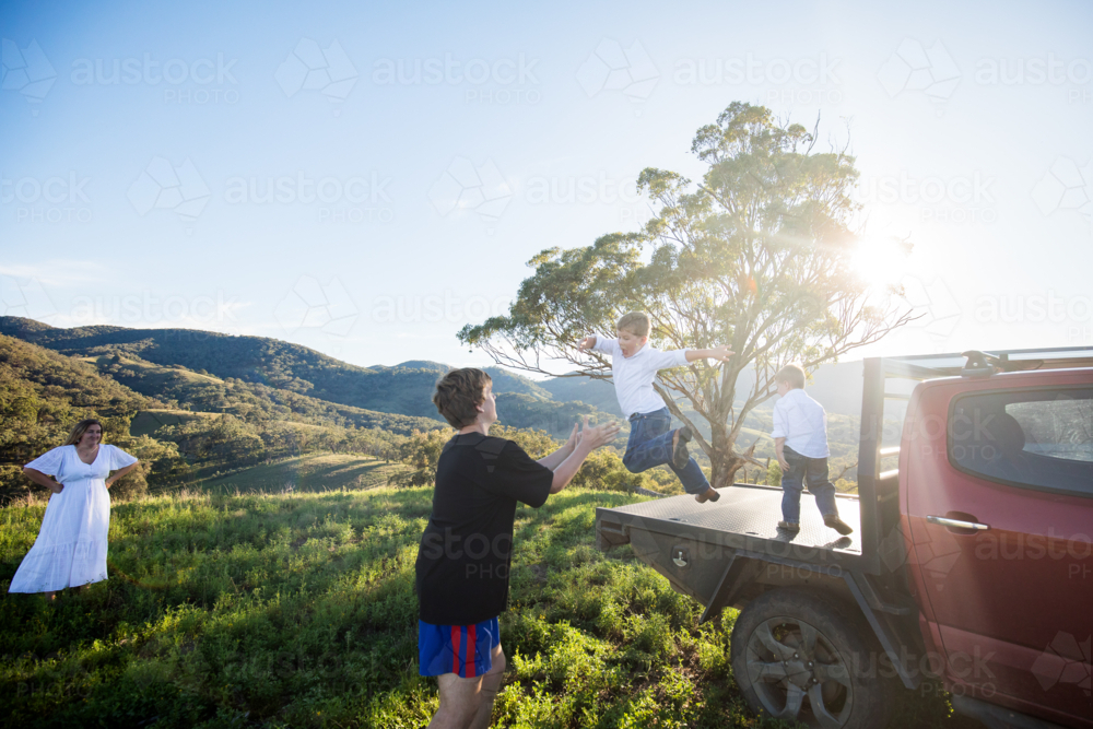 Image of Happy kids jumping off back of ute to teenage boy in the ...
