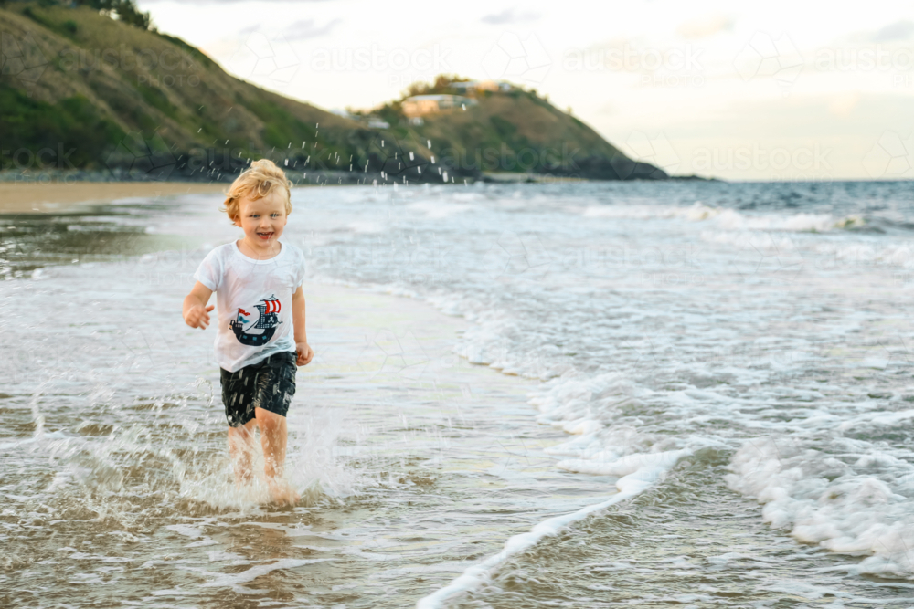 Image of Happy little boy running through shallow water at the beach ...