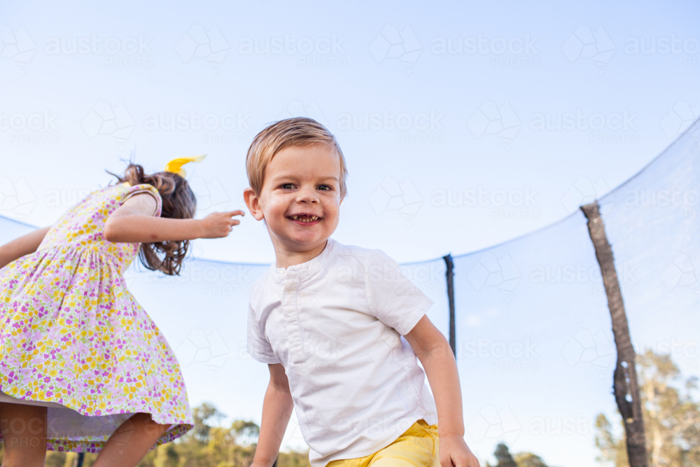 Image of Happy little boy smiling and jumping on trampoline with sister ...