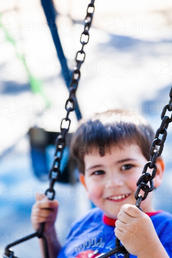 Image of Happy little boy swinging on a swing at the park - Austockphoto