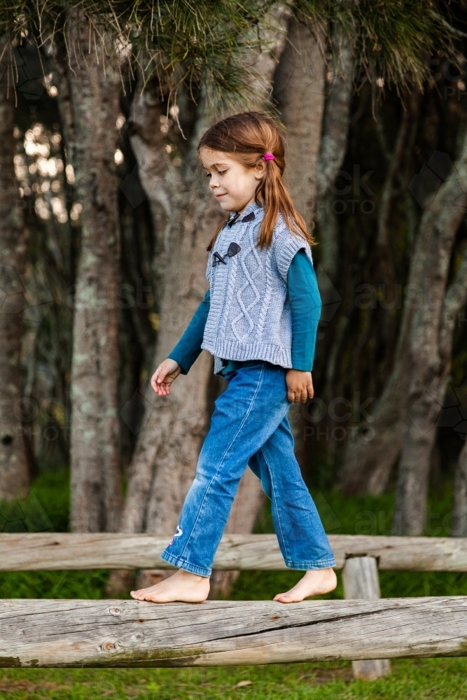 Image of Happy little girl balancing on a pole outside near forest ...