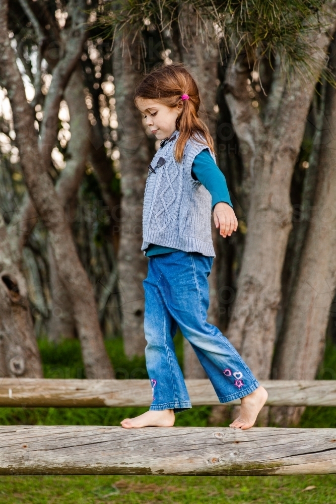 Image of Happy little girl balancing on a pole outside near forest ...