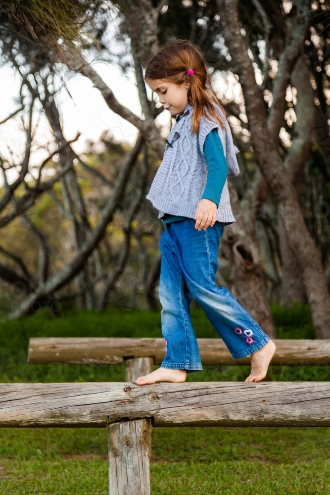 Image of Happy little girl balancing on a pole outside near forest ...