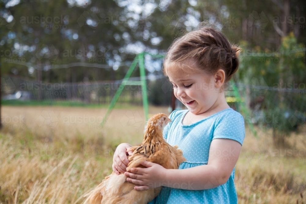 Image of Happy little girl holding pet chook on her lap outside ...