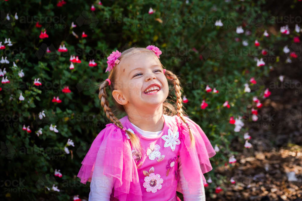 Image of Happy little girl in pink fancy dress in garden laughing up at ...