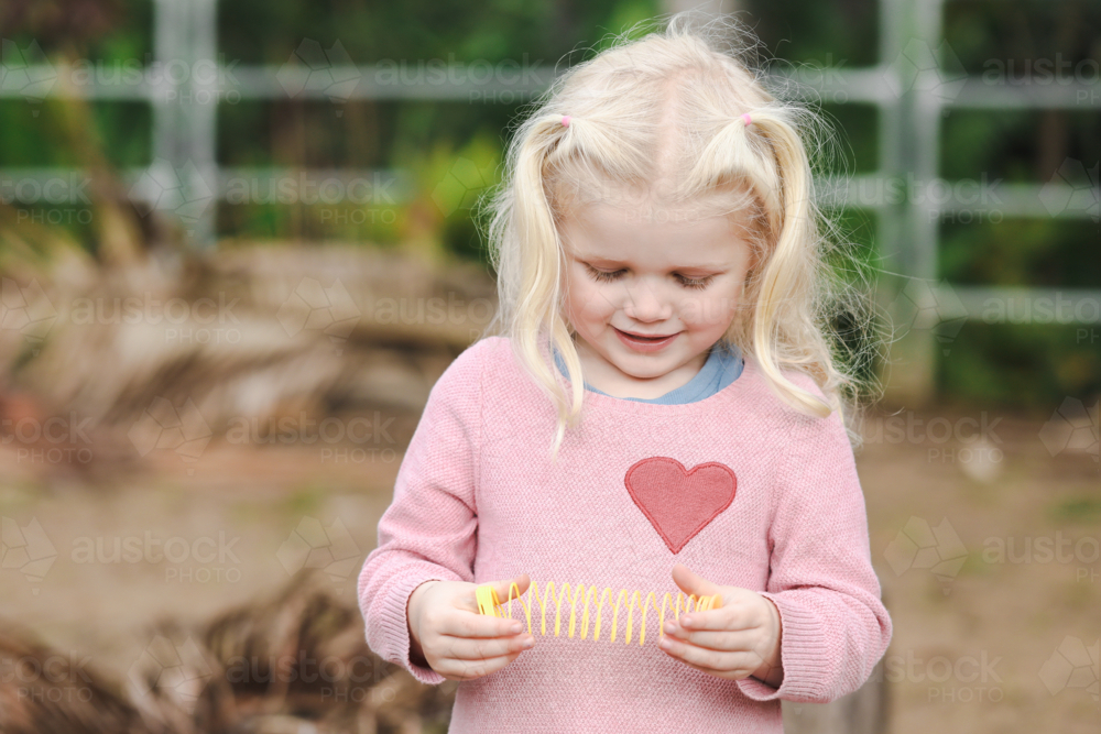 Image of Happy little girl playing with slinky toy in the garden ...