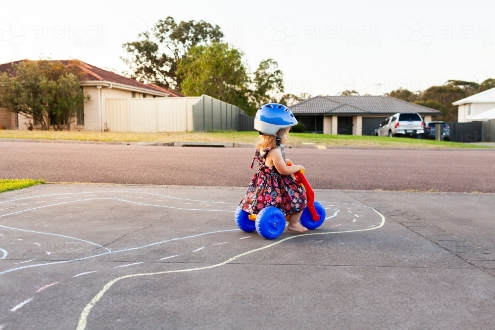 Image of Happy little toddler girl riding trike on chalk tracks drawn ...