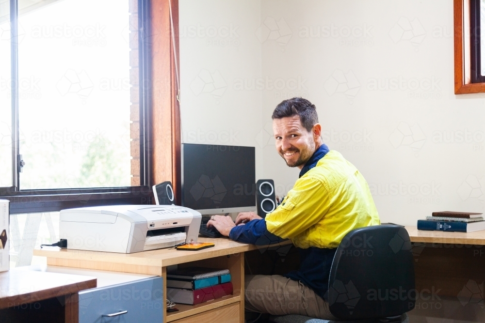 Image of Happy male tradie at computer in home office - Austockphoto